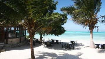 Um restaurante à beira-mar com mesas ao ar livre, palmeiras e vista para o oceano.