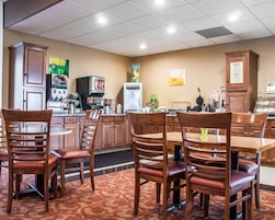 Uma sala de jantar de hotel com cadeiras de madeira, uma máquina de café, um refrigerador e um quadro de cardápio.