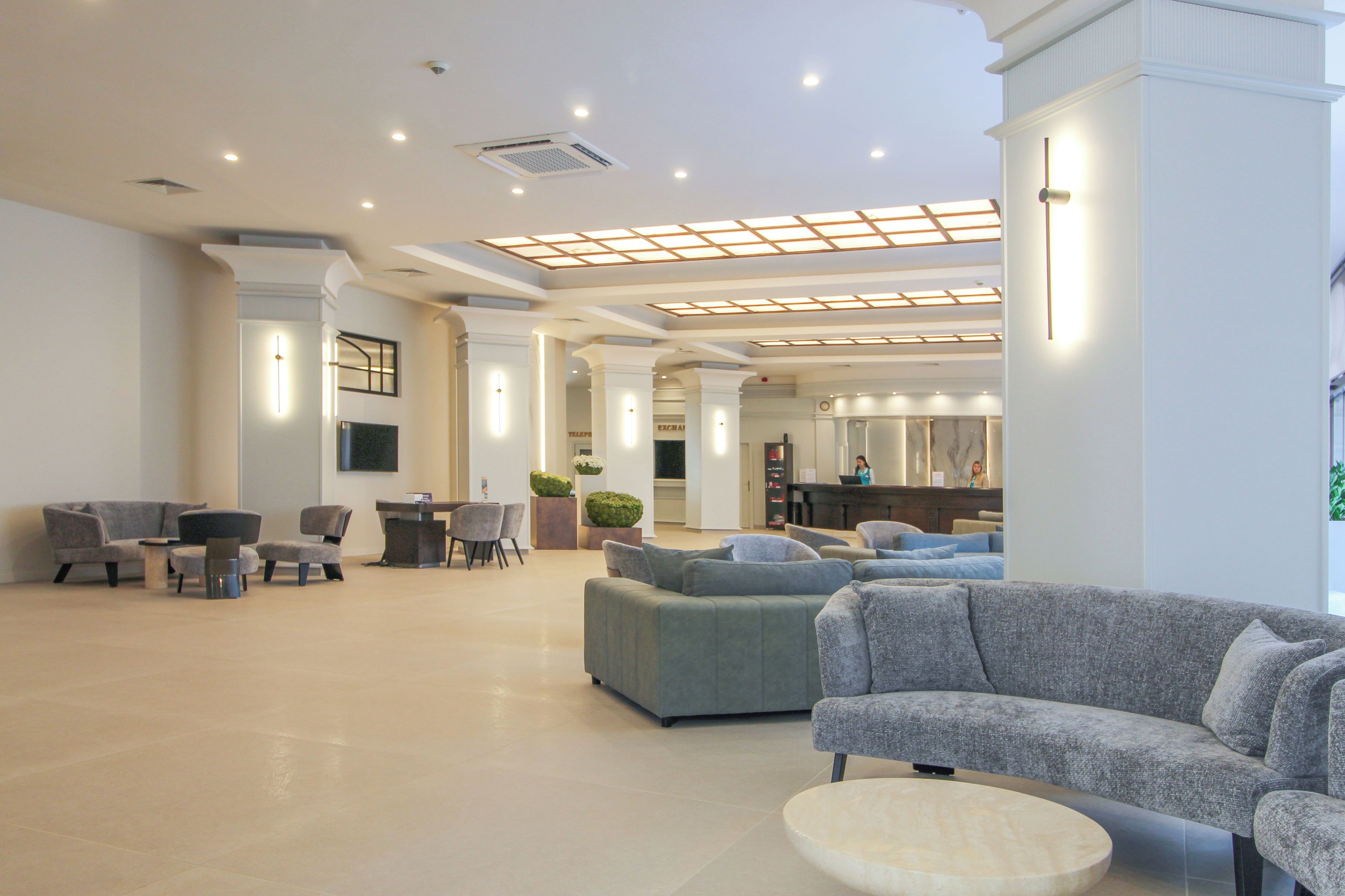 Um hall amplo com um sofá modular cinzento grande, uma mesa de centro redonda e uma área de estar com cadeiras e uma pequena mesa.