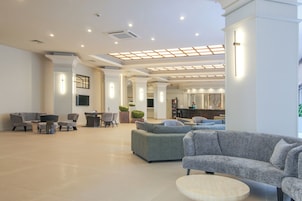 Um hall amplo com um sofá modular cinzento grande, uma mesa de centro redonda e uma área de estar com cadeiras e uma pequena mesa.