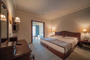 Quarto de hotel com uma cama grande, abajures, escrivaninha com cadeira, espelho e vista para o corredor.
