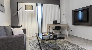 Uma sala de estar moderna com sofá, mesa de centro de vidro, escrivaninha com computador e televisão na parede.