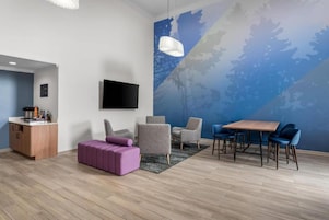 Uma sala de estar moderna com televisão de tela plana, uma mesa de jantar de madeira com cadeiras, um sofá roxo e uma poltrona cinza.