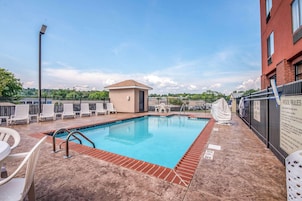 Piscina com borda de tijolos, espreguiçadeiras, um pequeno edifício e uma cerca.
