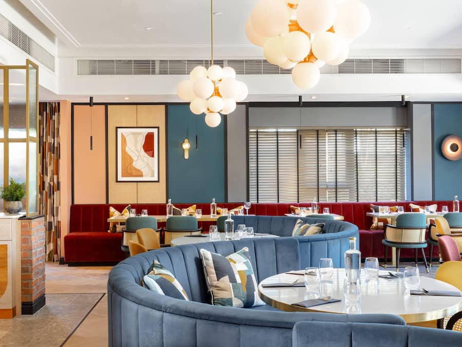 Um restaurante moderno com mesas redondas, assentos estofados em azul e iluminação decorativa.
