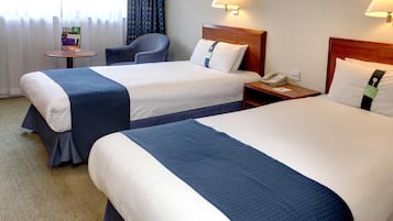 Quarto de hotel com duas camas, uma mesa de cabeceira com telefone e uma mesinha com abajur.