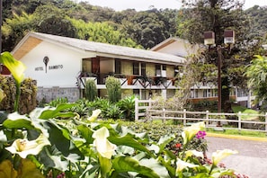 Hotel com fachada branca, varandas e vegetação exuberante em primeiro plano.