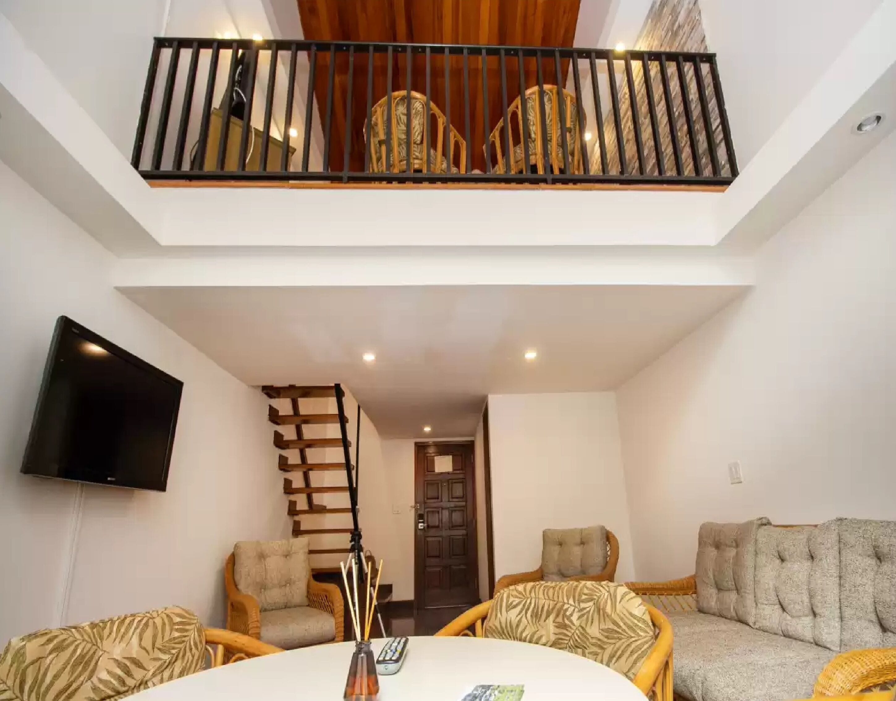 Uma sala de estar com televisão, móveis de madeira, uma escada e uma varanda.