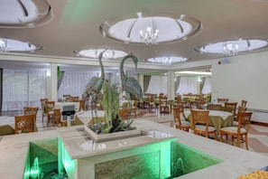 Uma ampla área de jantar com mesas e cadeiras, um centro de mesa decorativo e um candelabro.