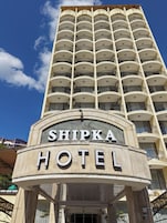 Um hotel com uma placa de destaque que diz 'SHIPKA HOTEL'. Apresenta uma construção de vários andares com varandas em cada andar.
