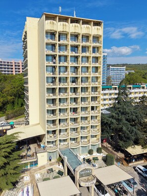 Um hotel com vários andares, varandas, piscina e uma placa com a inscrição 'Shipka Hotel'.