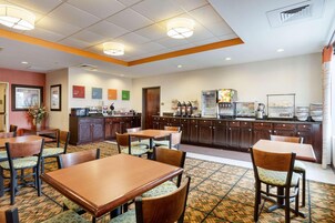 Uma sala de jantar de hotel com mesas e cadeiras, uma área de cozinha com eletrodomésticos e um chão estampado.
