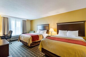Quarto de hotel com duas camas, uma escrivaninha, uma cadeira e uma janela com cortinas.