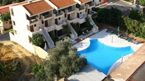 Um edifício de vários andares com piscina, rodeado por vegetação e vista para o mar.