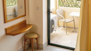 Quarto com um banco de madeira, um banquinho, um espelho e vista para uma varanda com uma cadeira e um ar condicionado.
