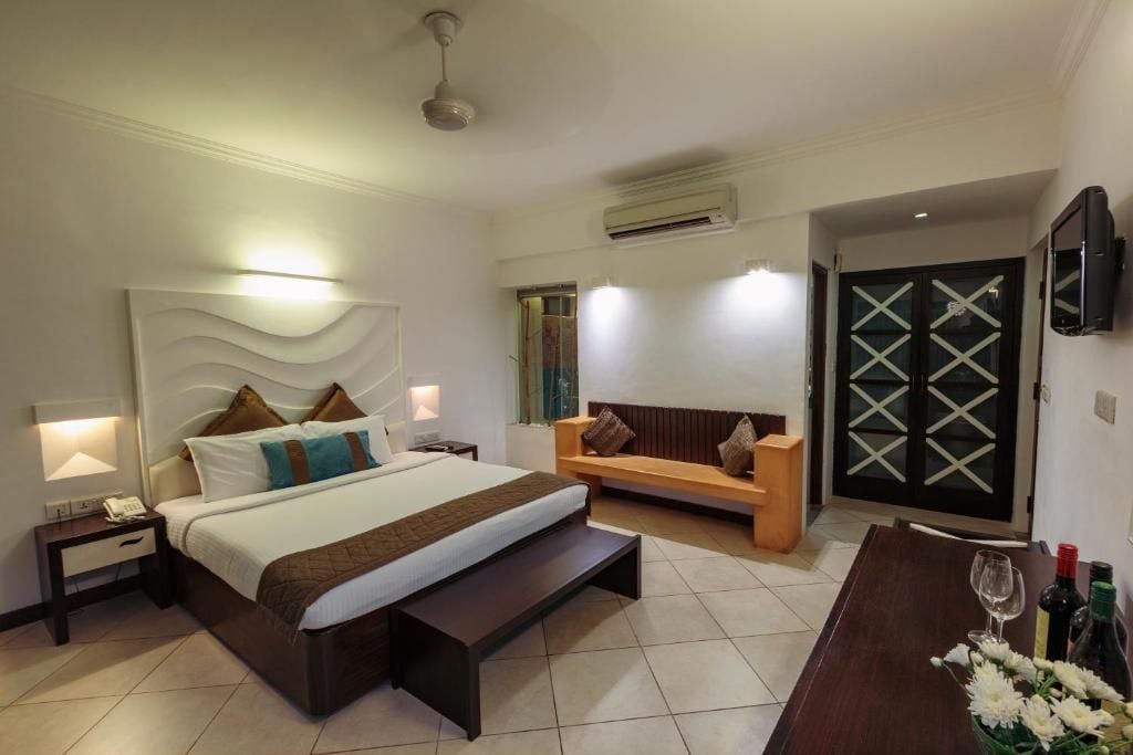 Quarto de hotel com cama, mesas de cabeceira, um banco, um sofá, uma TV e uma porta com janela.