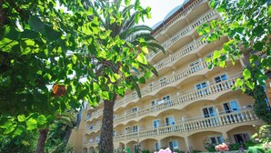 Um hotel com vários andares, varandas, uma palmeira e uma rosa em primeiro plano.
