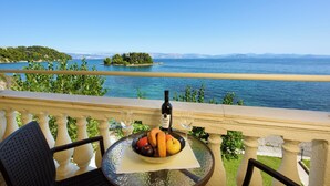Uma mesa com uma tigela de frutas e uma garrafa de vinho, com vista para um corpo d'água e uma ilha ao longe.