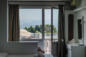 Quarto com uma grande janela com vista para a água e montanhas ao longe.