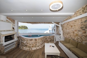 Quarto aconchegante com lareira de pedra, parede de pedra, vista para o mar e luminária branca no teto.
