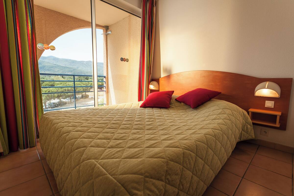 Quarto de hotel com uma cama, mesa de cabeceira, abajur e vista para o exterior.