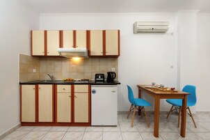 Uma cozinha compacta com armários de madeira, uma máquina de lavar louça embutida, uma cafeteira e uma mesa de jantar com cadeiras azuis.