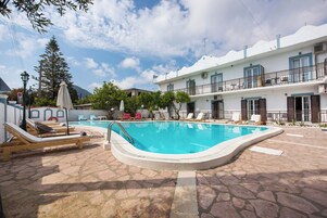 Piscina com espreguiçadeiras, um pátio de pedra e um edifício com varandas.