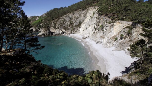 Paisagem costeira com praia, águas cristalinas e falésias rochosas.