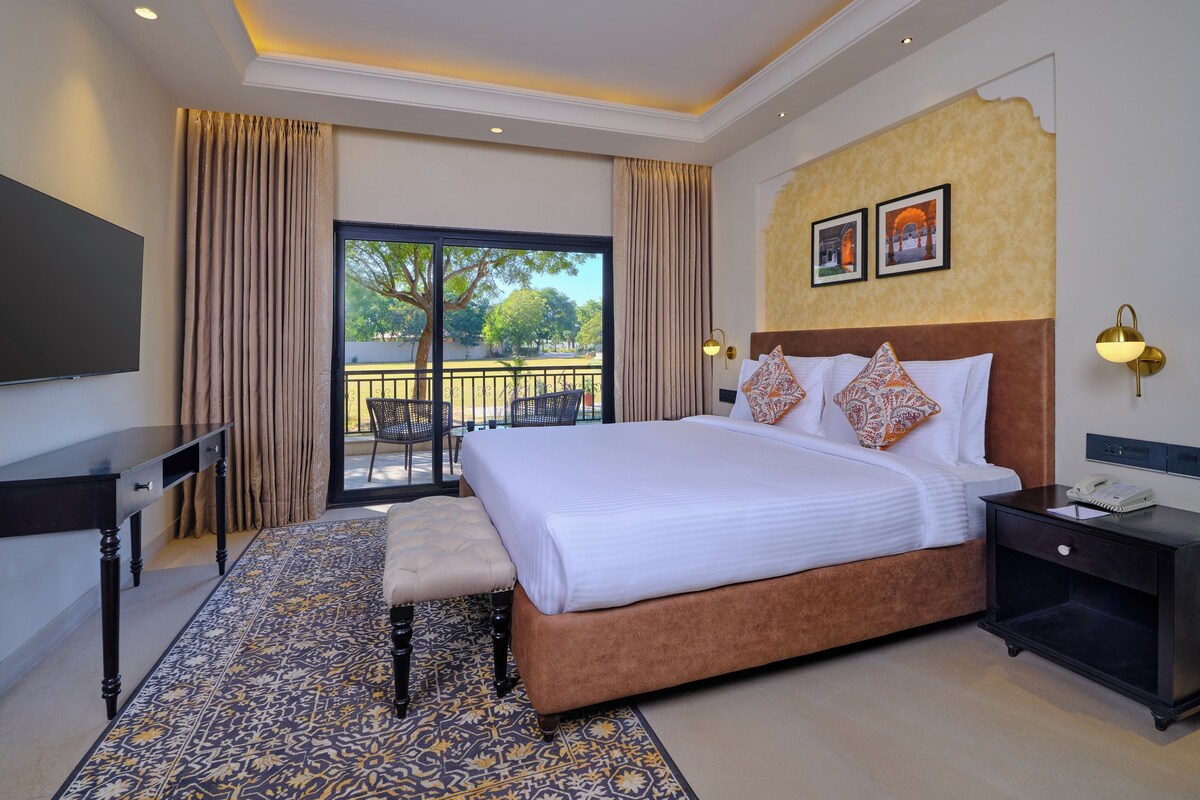 Quarto de hotel com uma cama grande, uma escrivaninha, uma cadeira, uma mesinha, telefone e varanda com vista para árvores.