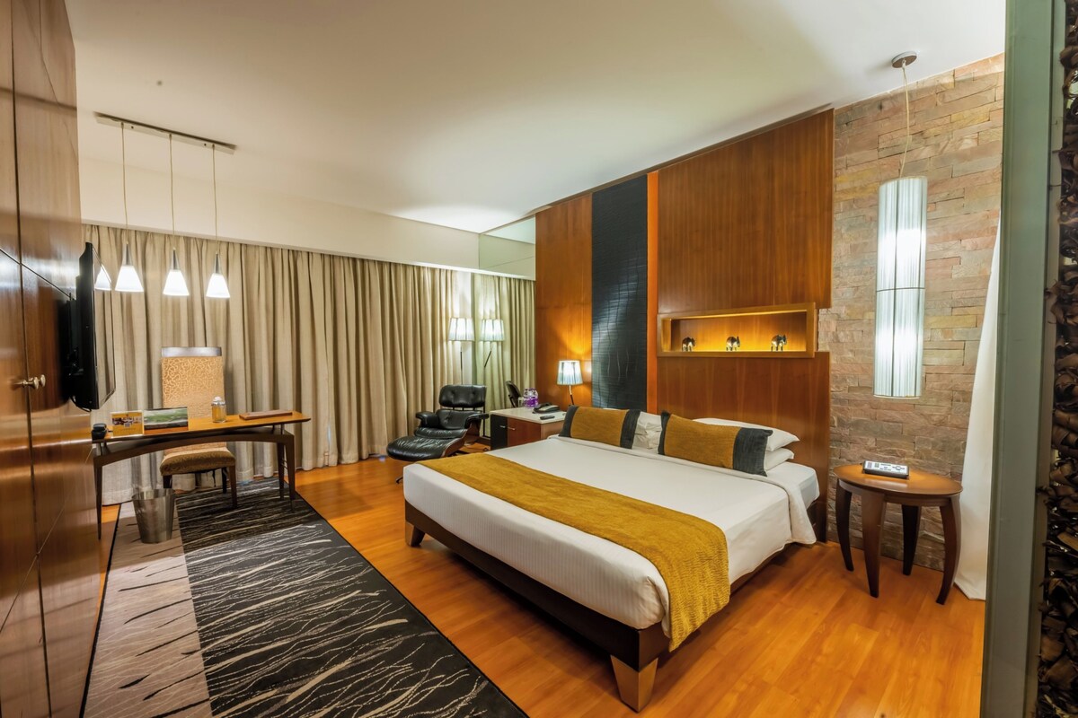 Quarto de hotel moderno com uma cama grande, uma escrivaninha, uma cadeira, uma TV e uma parede com detalhes em pedra.