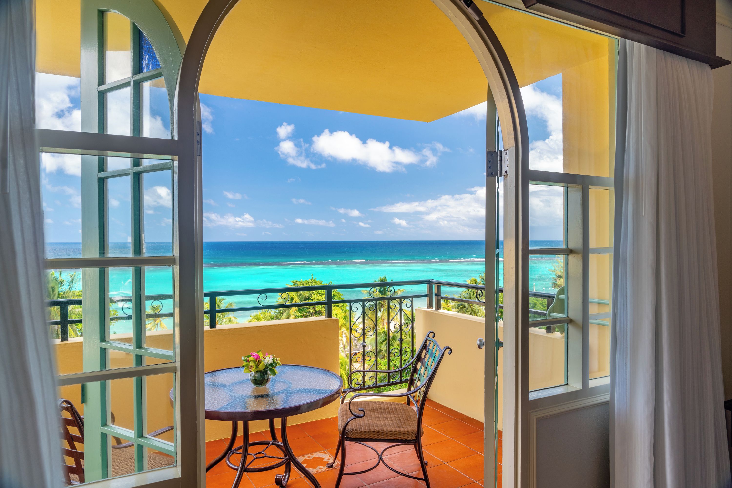 Varanda com vista para o oceano, uma mesa com um vaso de flores e uma cadeira.