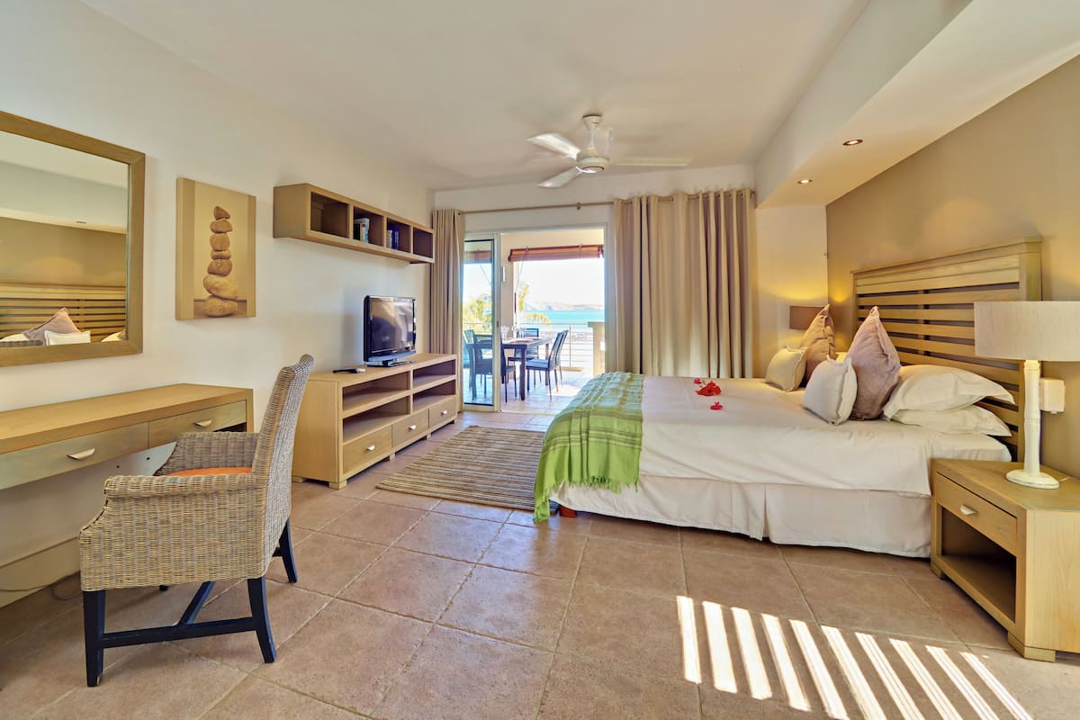 Quarto de hotel com cama, escrivaninha, poltrona, televisão e varanda com vista.