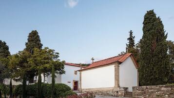 Um edifício branco com telhado de telhas vermelhas, rodeado por árvores e um muro de pedra.