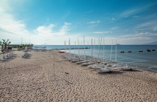 Uma praia com fileiras de barcos à vela, uma torre de salva-vidas e céu claro.