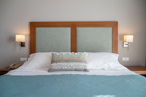 Cama bem arrumada com manta azul, duas almofadas com desenho estampado e cabeceira de madeira.