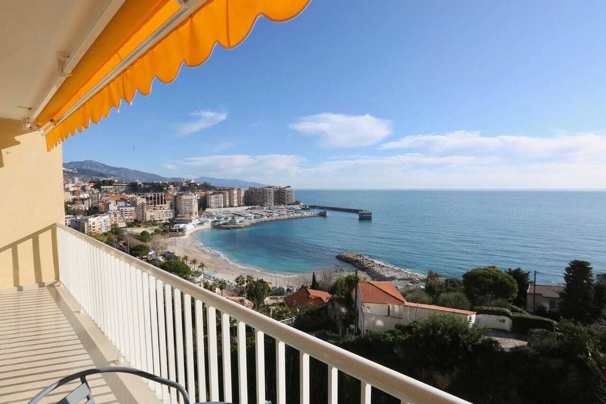 Uma varanda com vista para uma vila costeira, uma praia e um cais.