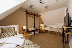 Quarto de hotel com cama de dossel, uma cama simples, escrivaninha com televisão e ventoinha de teto.