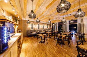 Restaurante com piso de madeira, luminárias negras pendentes e um espaço de bar.