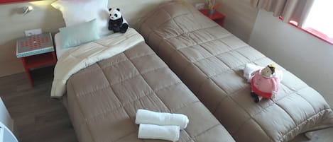 Quarto de hotel com duas camas, uma mesa de cabeceira, uma cadeira vermelha, um brinquedo de pelúcia de panda e uma boneca.
