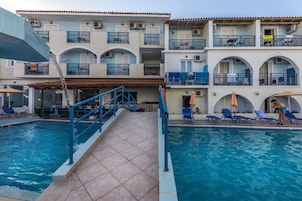 Piscina com uma escadaria azul que leva a uma área coberta, cercada por edifícios com varandas e áreas de estar ao ar livre.