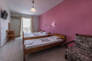 Quarto com duas camas de madeira, uma cadeira de madeira, um banco e uma televisão fixada na parede.