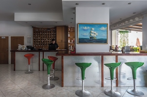 Um espaço de bar com um bartender, uma pintura de um navio e vista para o exterior.