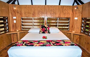 Quarto de madeira com uma cama, duas mesas de cabeceira e uma janela com persianas.