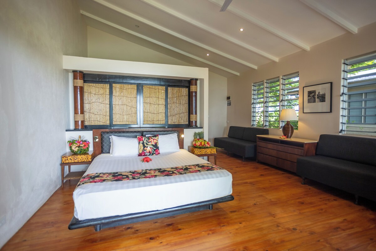 Um quarto de hotel espaçoso com uma cama grande, um sofá, uma mesa e uma janela com persianas.