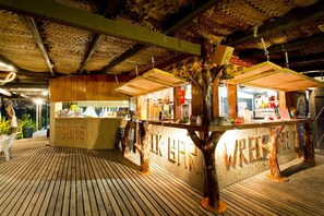 Uma área de bar com piso de madeira, um balcão com a placa 'TOURS' e uma estrutura em forma de árvore.