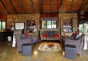 Uma sala de estar com paredes de pedra, móveis de vime, telhado de palha e lareira de pedra.