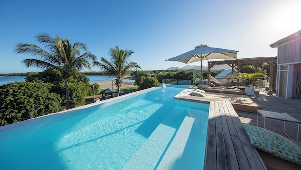 Piscina com vista para o mar, rodeada por palmeiras e espreguiçadeiras.