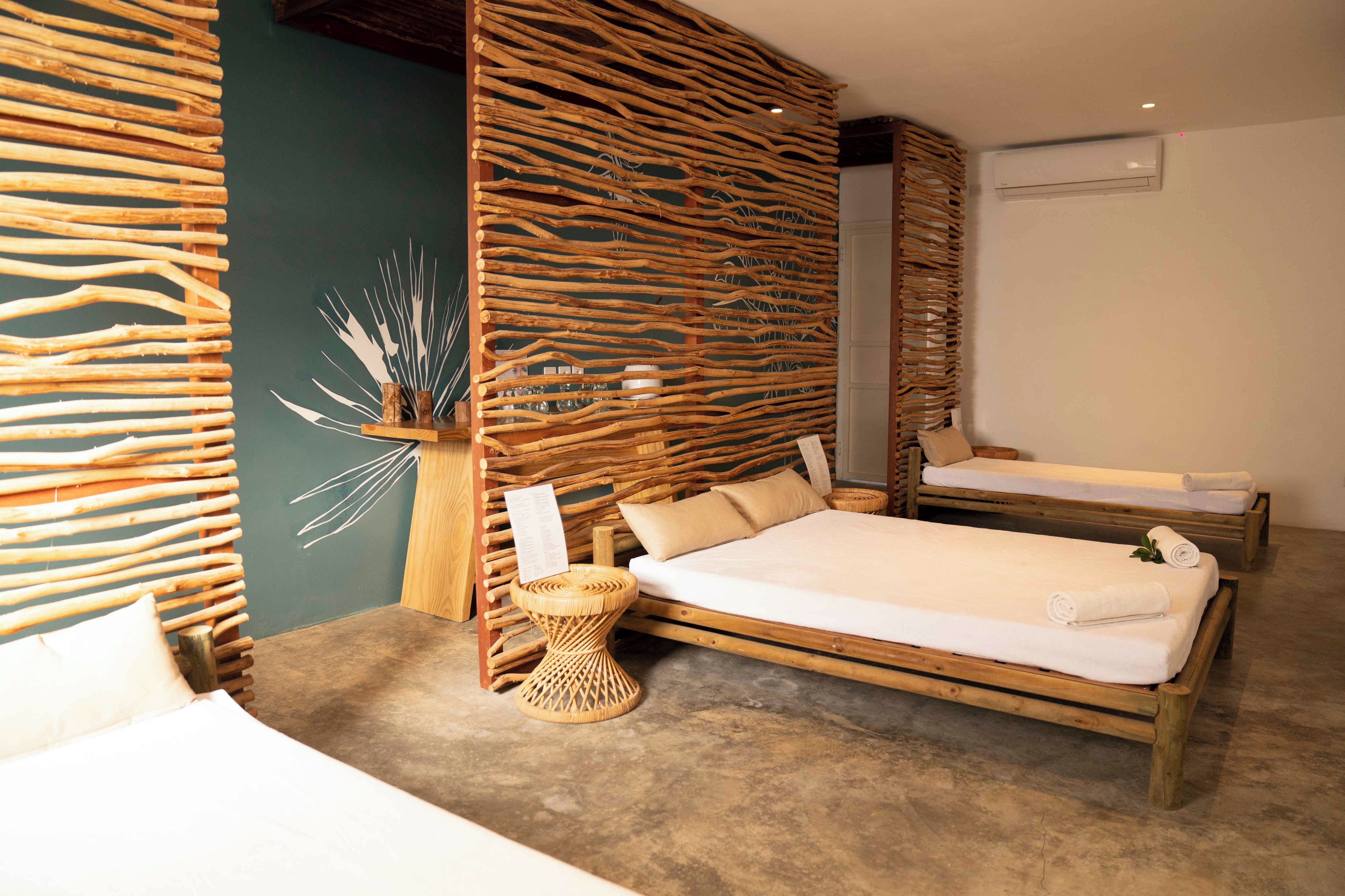 Quarto com duas camas de madeira, um divisório de fibra natural e uma pequena mesa redonda com um vaso.