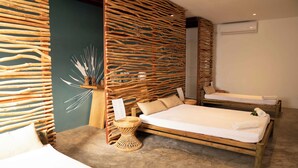 Quarto com duas camas de madeira, um divisório de fibra natural e uma pequena mesa redonda com um vaso.