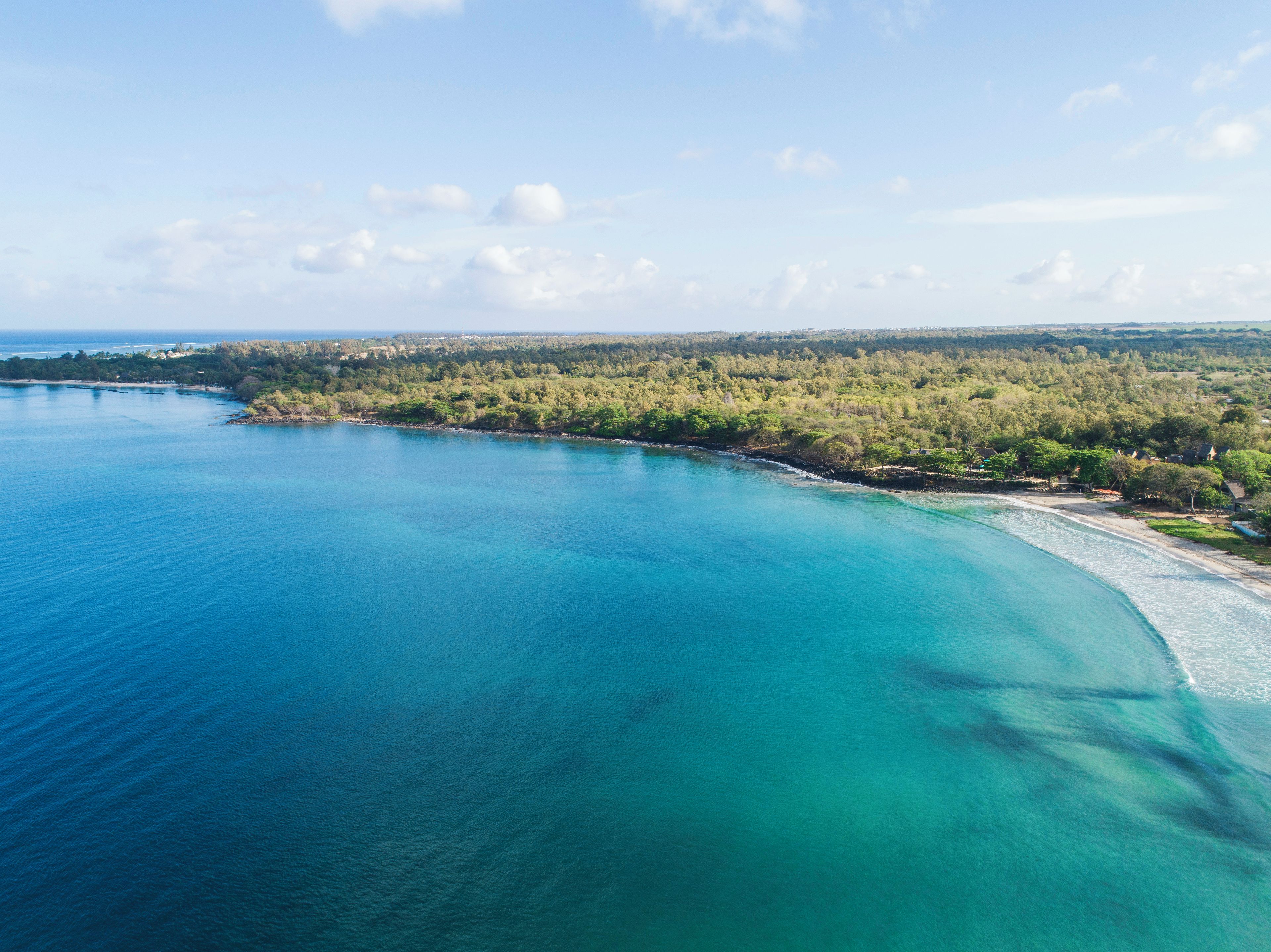 Vista aérea de uma área costeira com águas turquesa cristalinas, uma praia arenosa e uma península densamente arborizada.